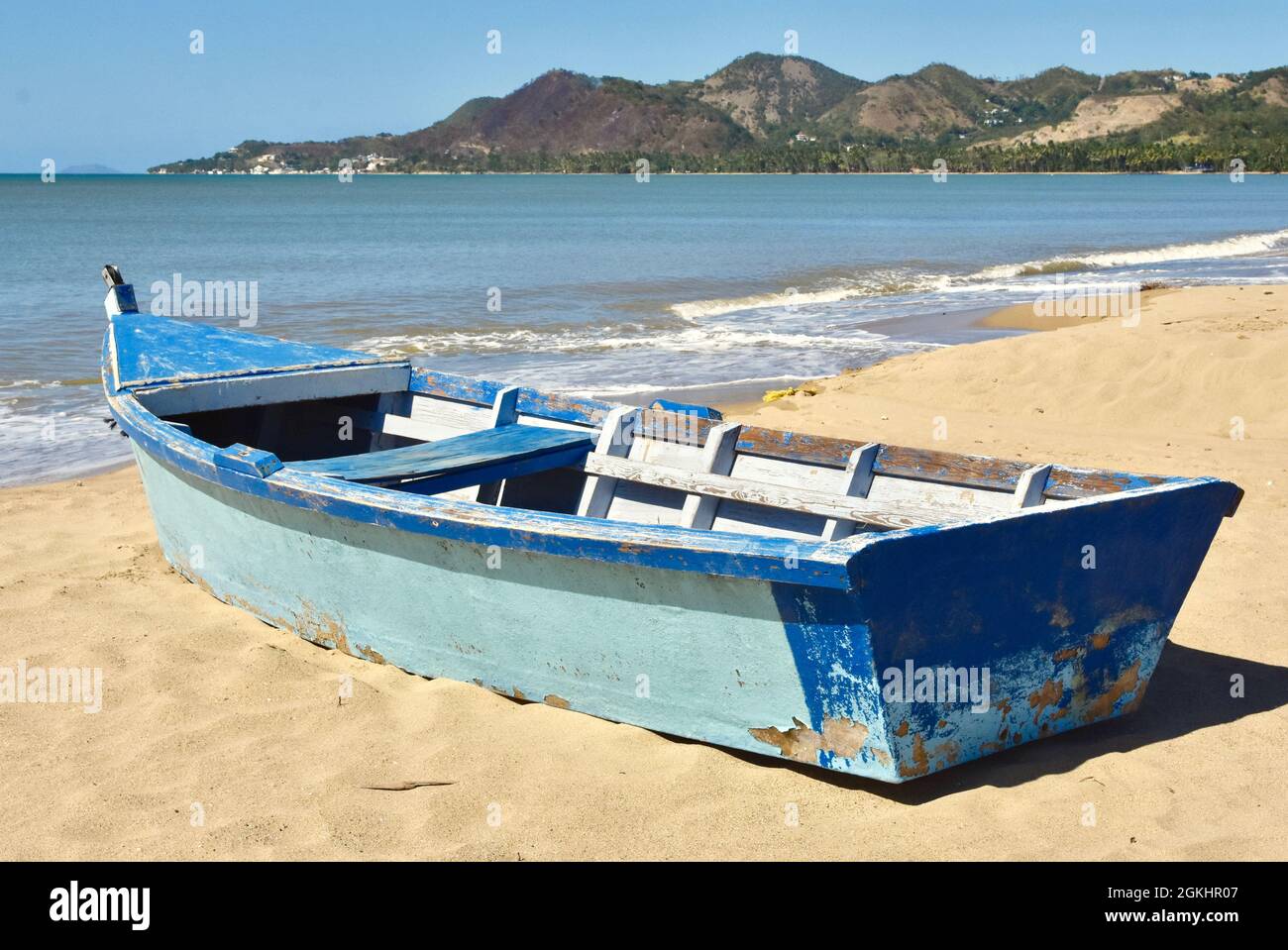 A small traditional Caribbean fishing boat on a sand beach with hills ...