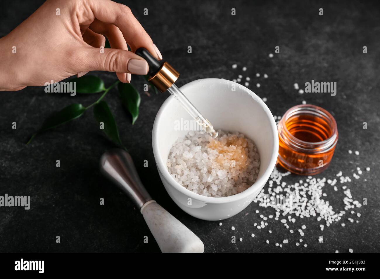 Woman dripping oil into bowl with sea salt on dark background Stock ...
