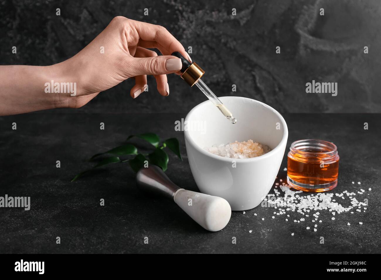 Woman dripping oil into bowl with sea salt on dark background Stock ...
