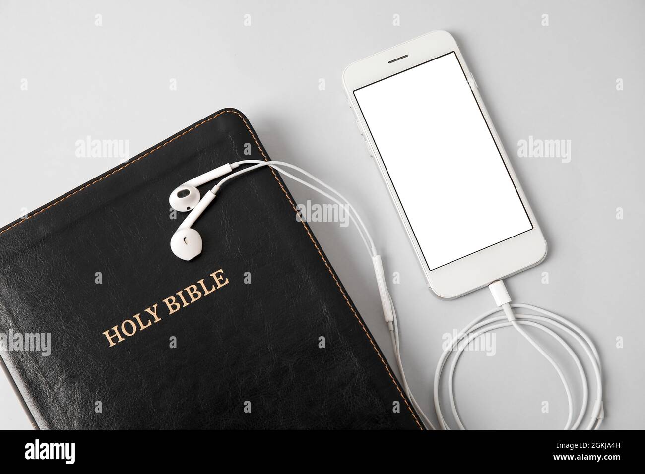 Holy Bible, mobile phone and earphones on light background, closeup ...