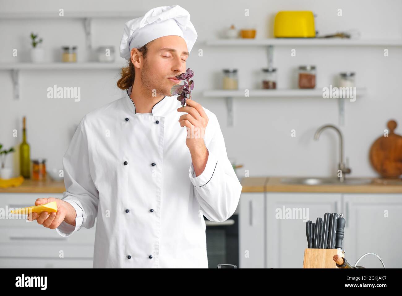 Handsome chef with cheese smelling basil in kitchen Stock Photo - Alamy