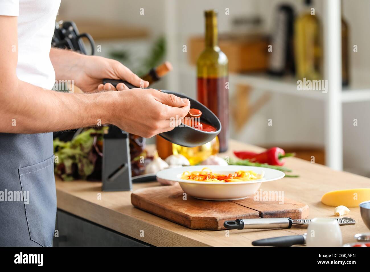 Male chef adding tasty sauce into plate with pasta in kitchen, closeup ...