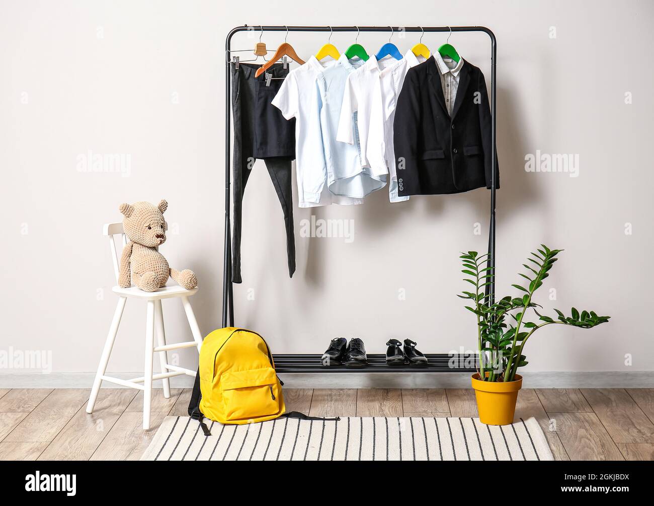 Rack with stylish school uniform and chair near light wall Stock Photo ...