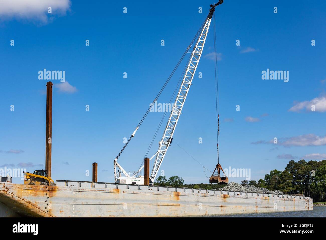 A clamshell bucket moves to pick up rocks from a barge to place in the ...