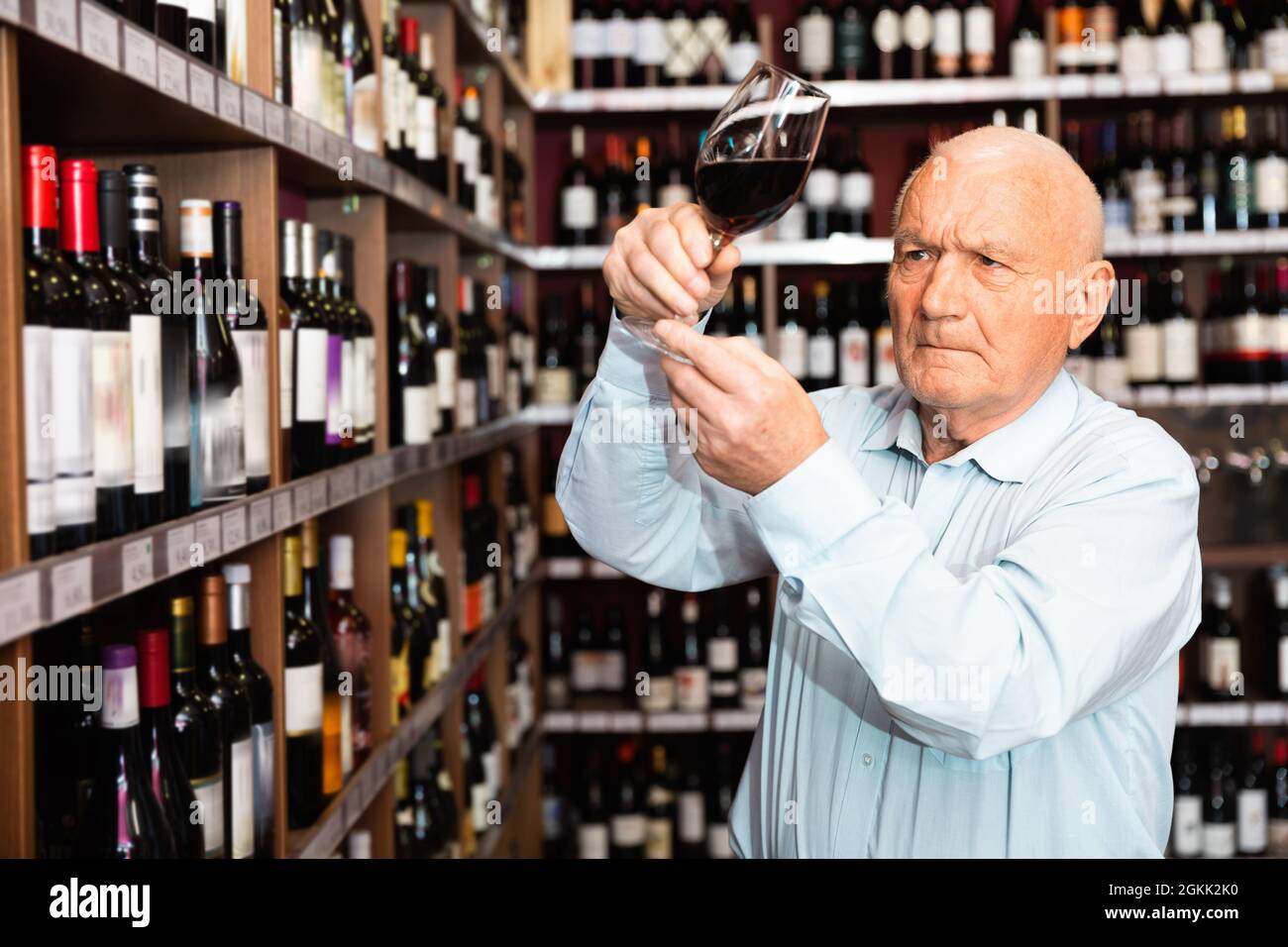 Older man inspecting quality of red wine in wine store in search of ...