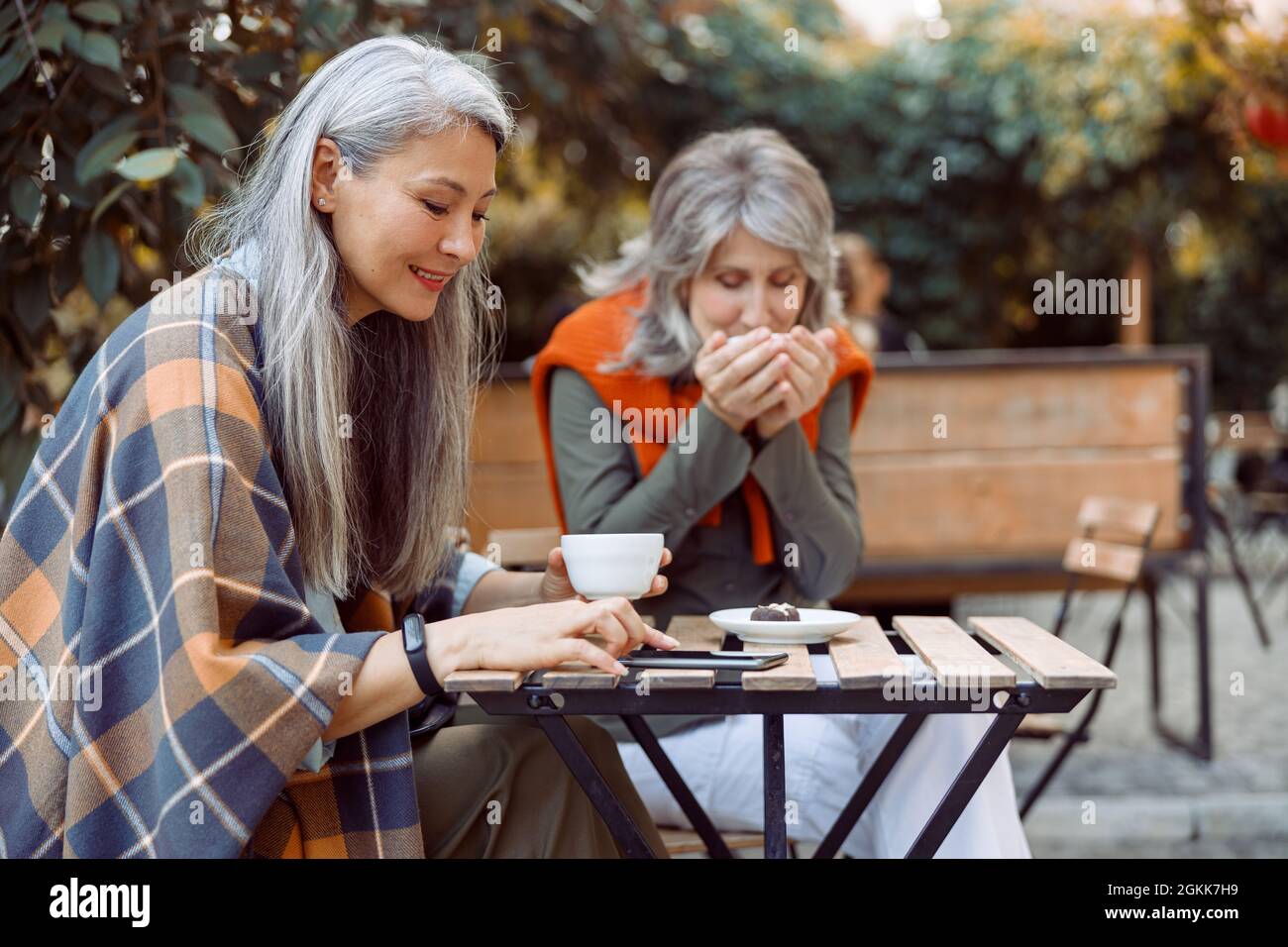 Senior Asian woman uses mobile phone while hoary haired friend drinks ...