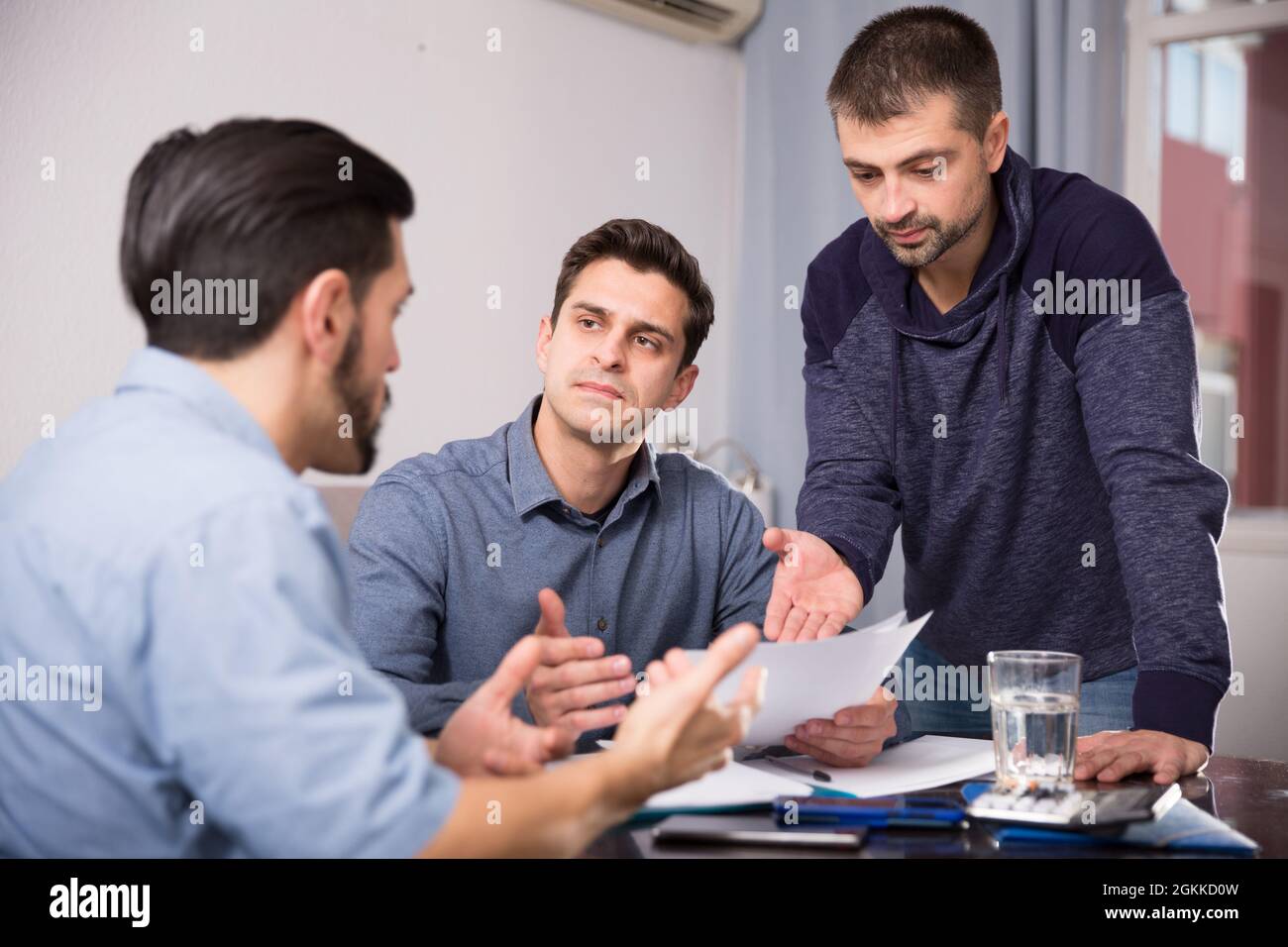 Three upset males with papers at table Stock Photo - Alamy