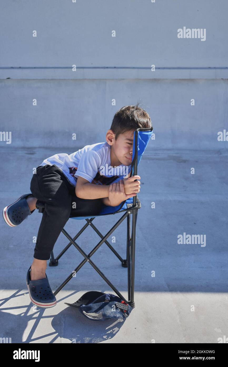 angry brunette boy lying on a blue deck chair, leaning his face against ...