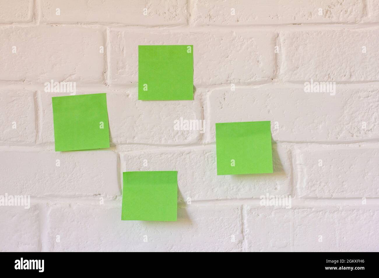 There are several green sticky notes hanging on the white brick wall ...