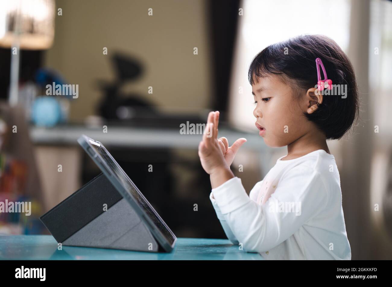 Shallow focus of a cute Thai girl using a tablet during her online ...
