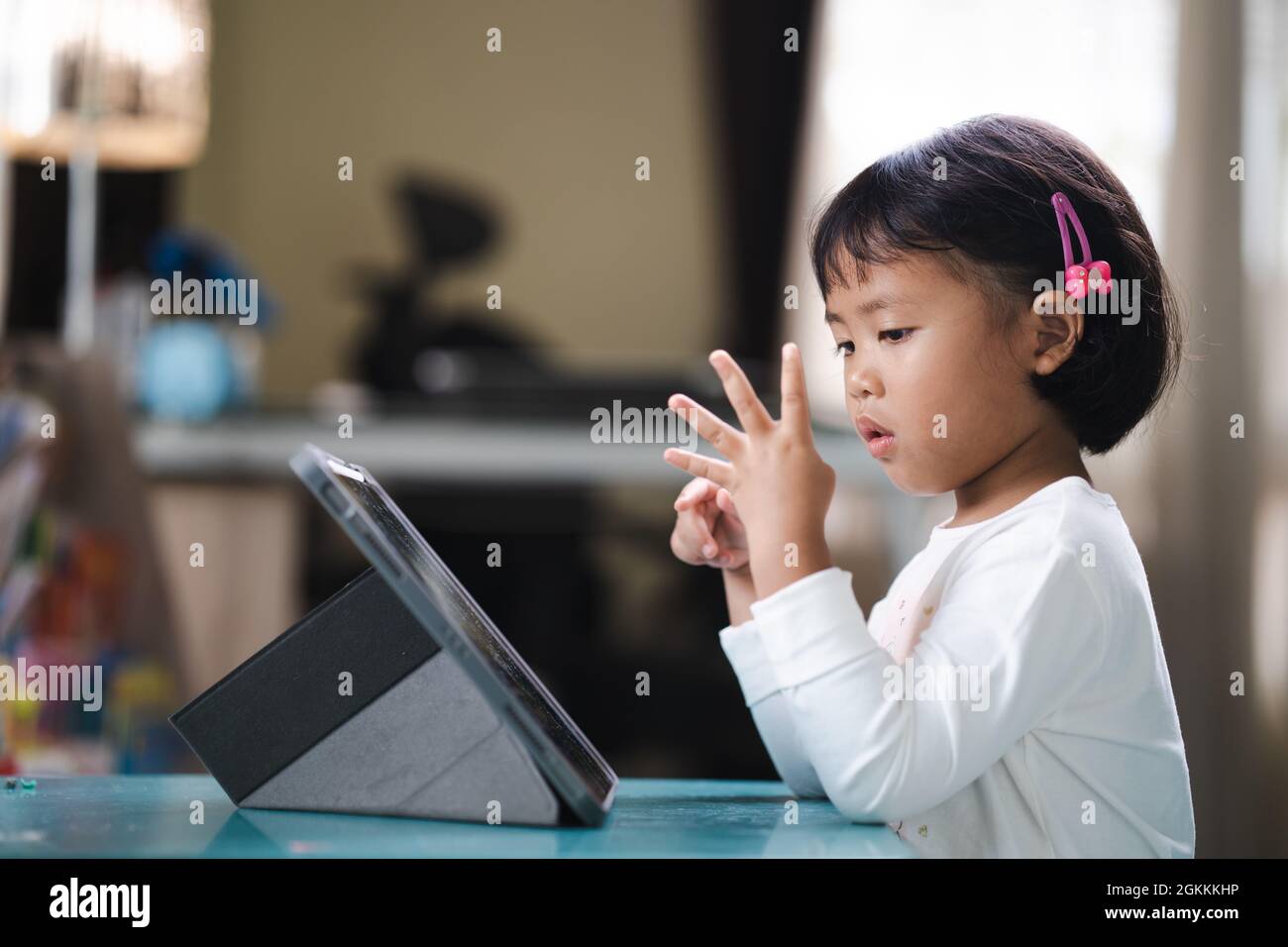 Shallow focus of a cute Thai girl using a tablet during her online ...