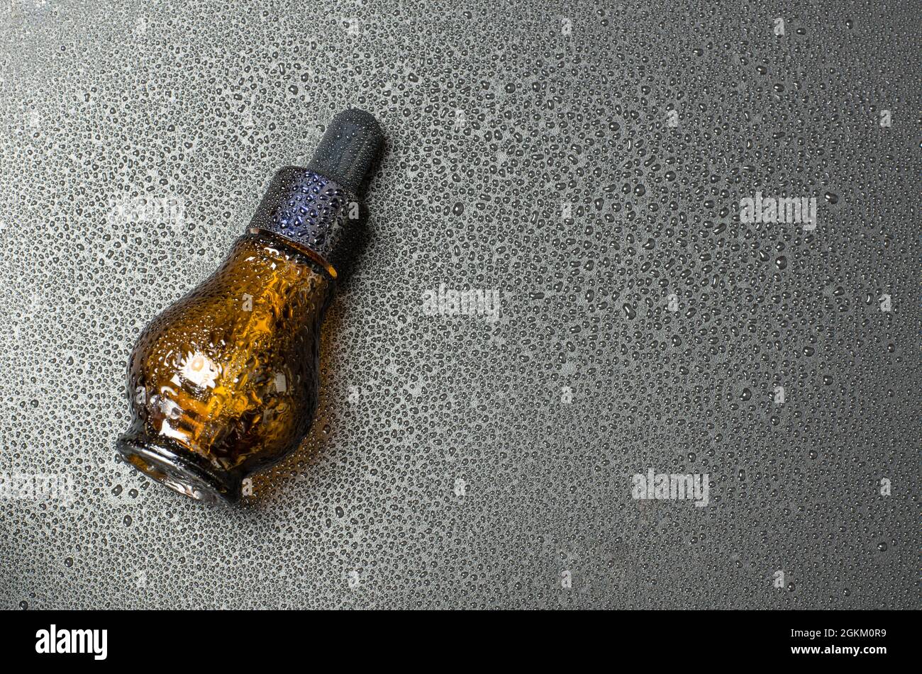Bottle with natural body oil on a black background with drops of foda ...