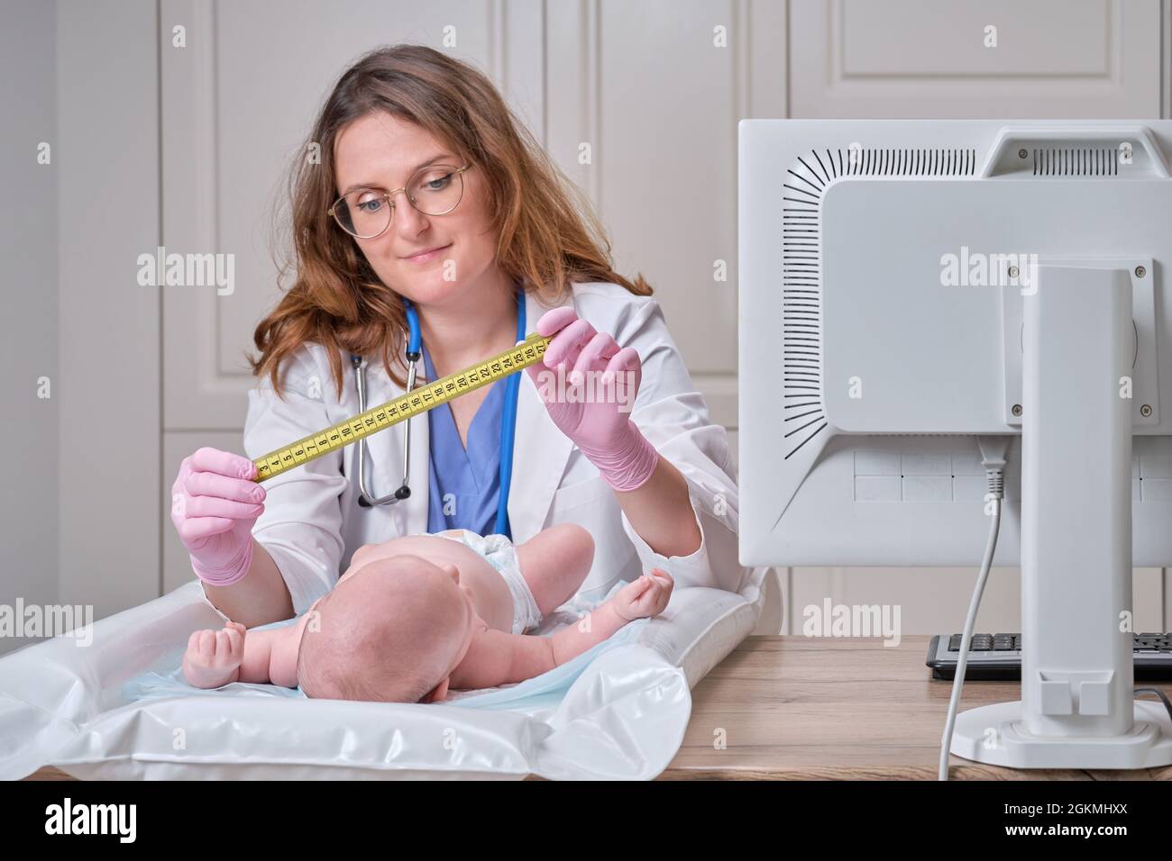 Doctor measures the growth of a newborn baby. A nurse in uniform checks ...