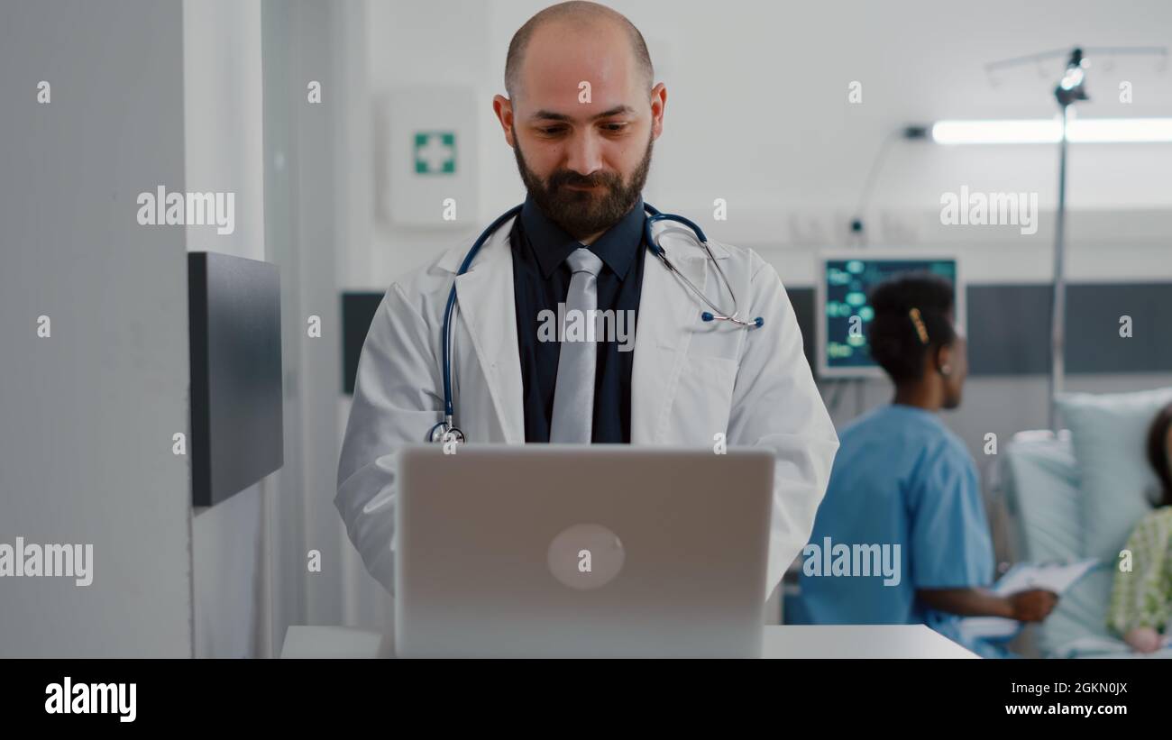 Front view of practitioner doctor typing illness expertise on computer ...