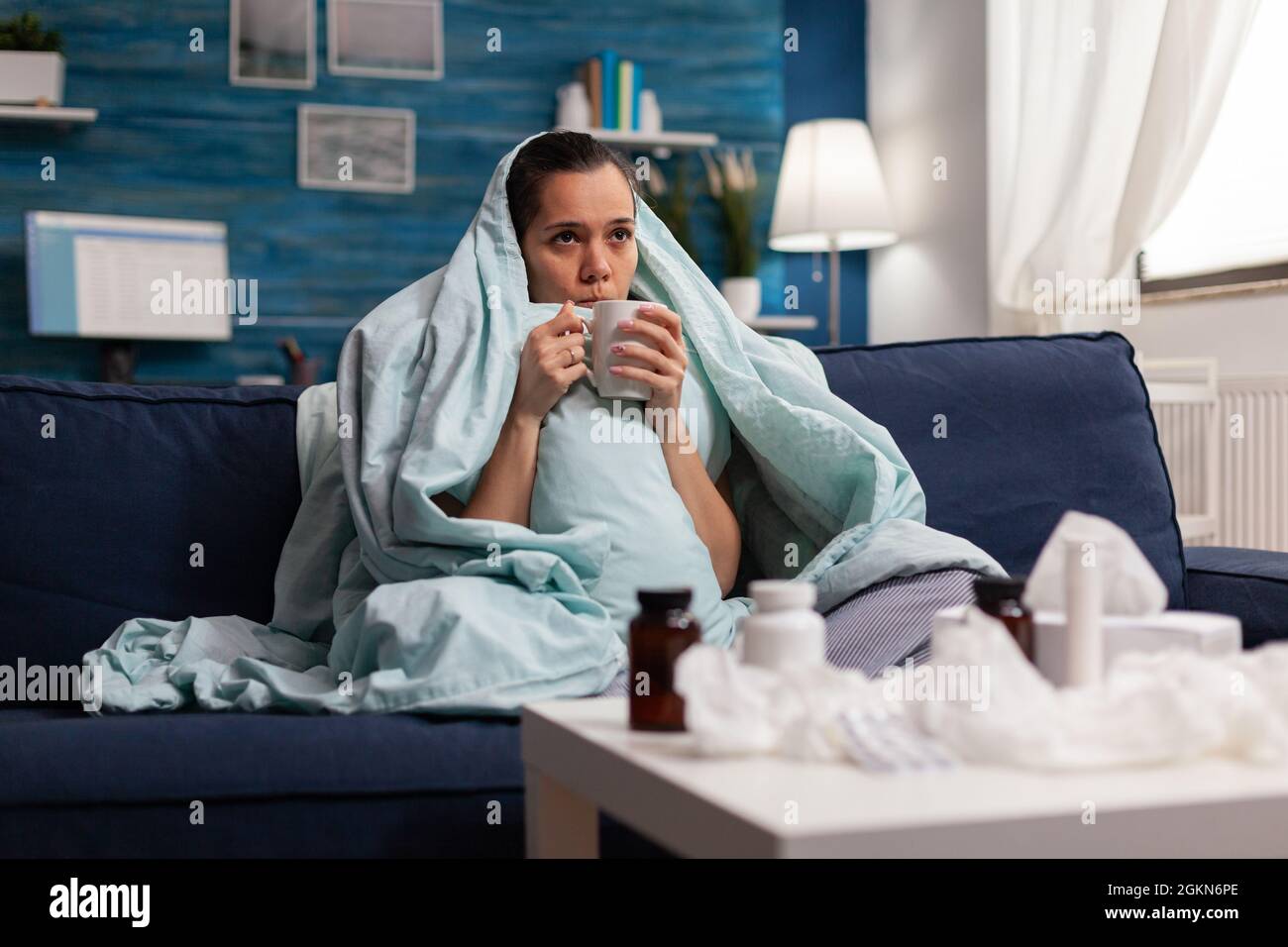 Woman feeling sick in blanket with warm drink at home having seasonal ...