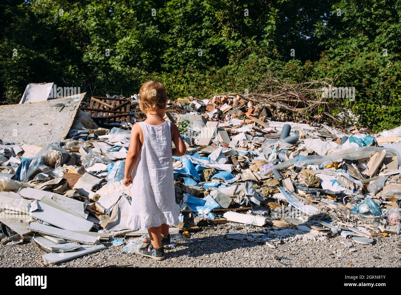 Little girl at a dump among a heap of scattered garbage in the forest ...
