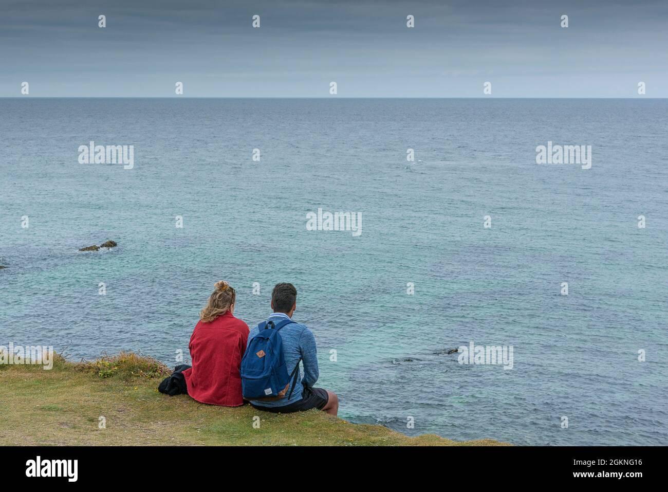A couple on holiday sitting together on the coast in Newquay ...