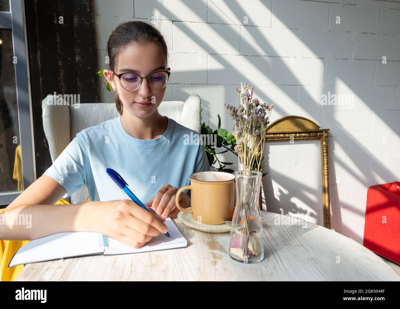 Pensive girl student writes with a pen an assignment in a notebook ...