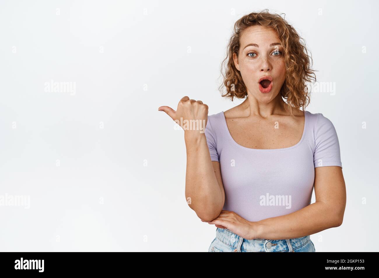 Amazed blond girl drop jaw, pointing finger left and looking in awe ...