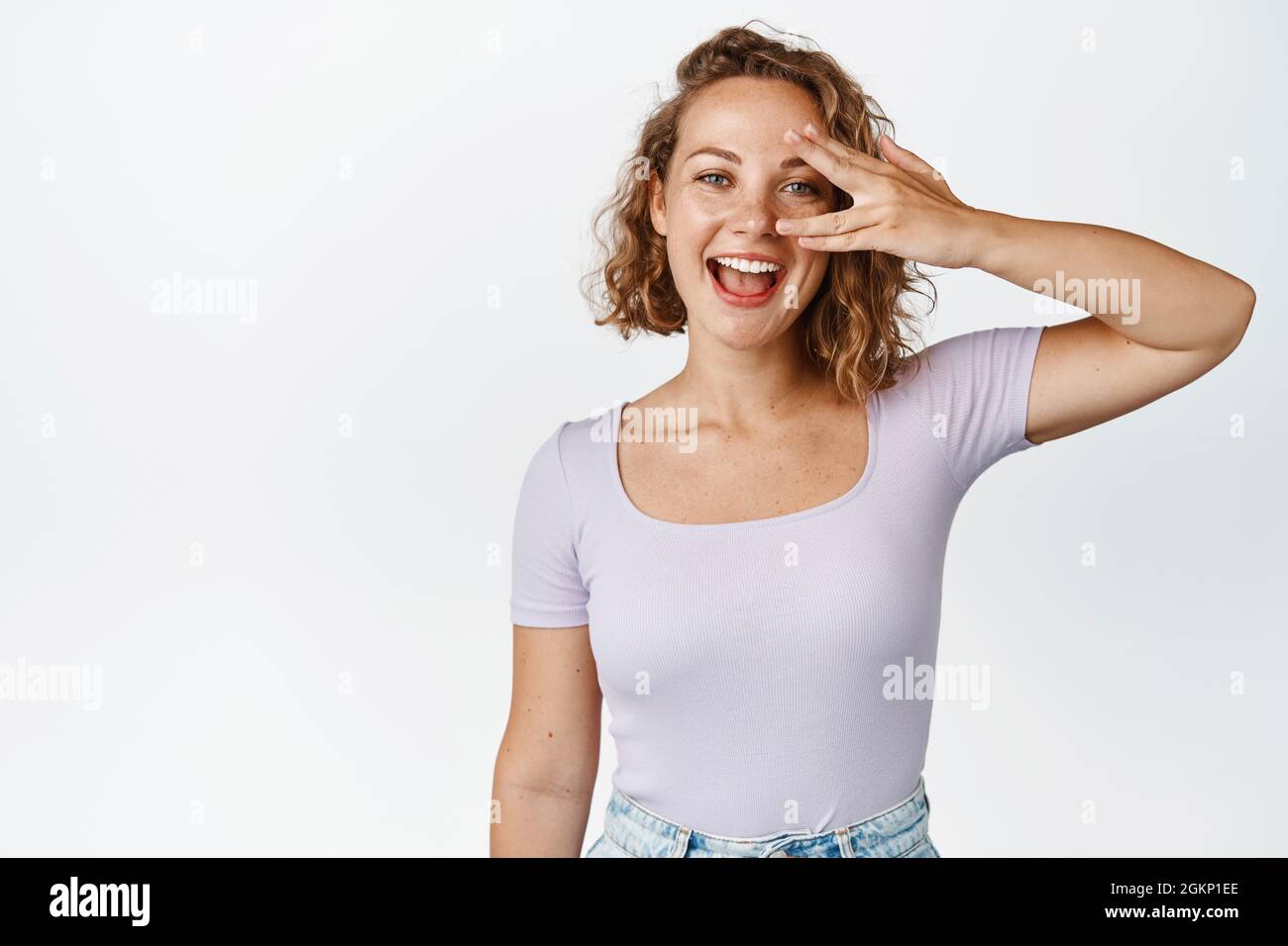 Beautiful blond girl showing eye peace gesture, laughing and smiling ...