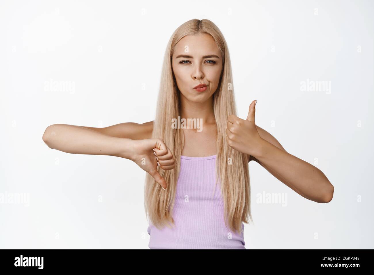 Unsure blond woman showing thumbs up and down, looking puzzled ...