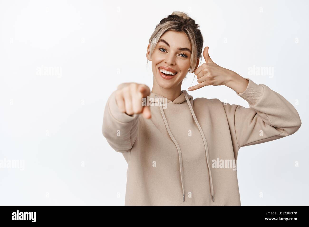 Young blond woman pointing finger at camera, showing mobile phone ...