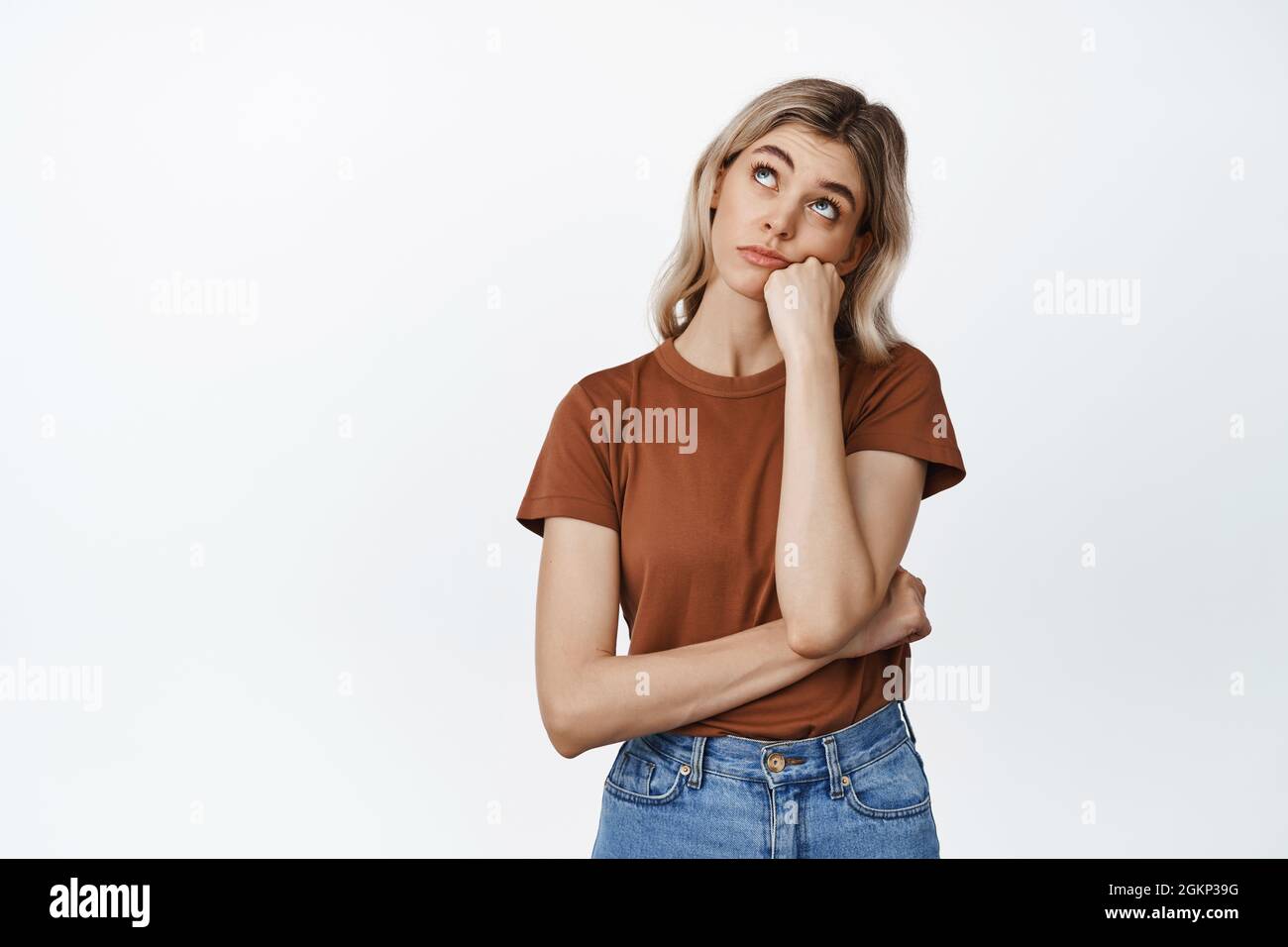Thoughtful girl looking up with bored face expression, standing in ...