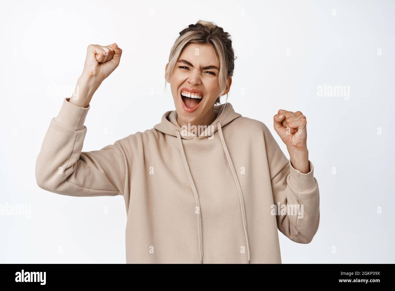 Winning. Young happy woman shouting encouraged, raising clenched fists ...
