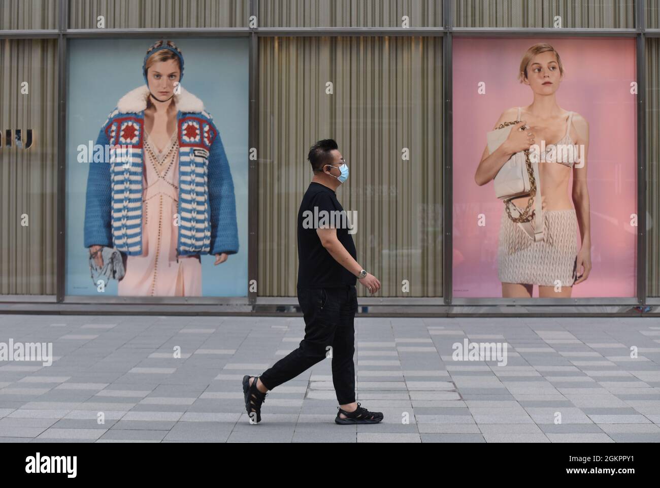A pedestrian wearing a mask walks by a huge commercial poster on ...
