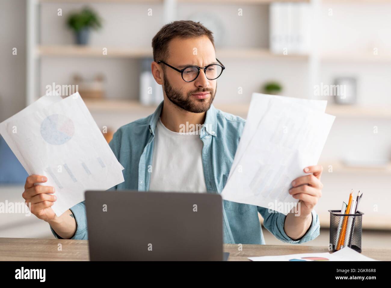 Serious young man looking through documents while having online ...