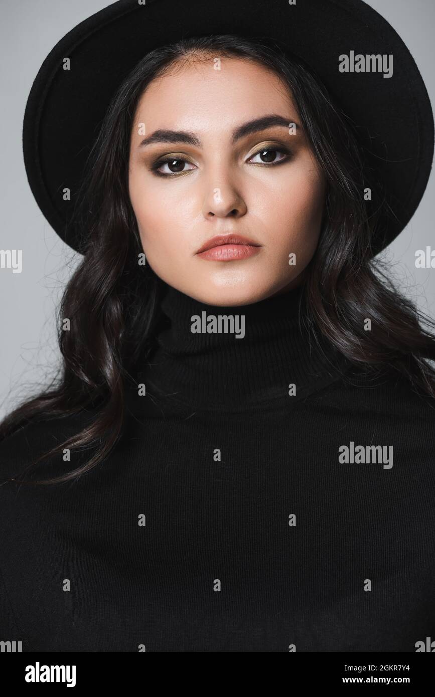 pretty model in black fedora hat and turtleneck looking at camera isolated on grey Stock Photo ...