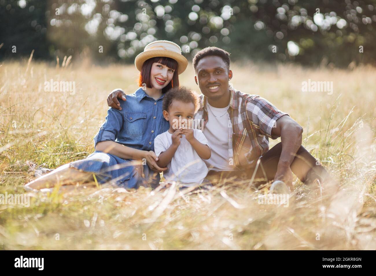 Positive multicultural parents sitting with little son on grass and ...