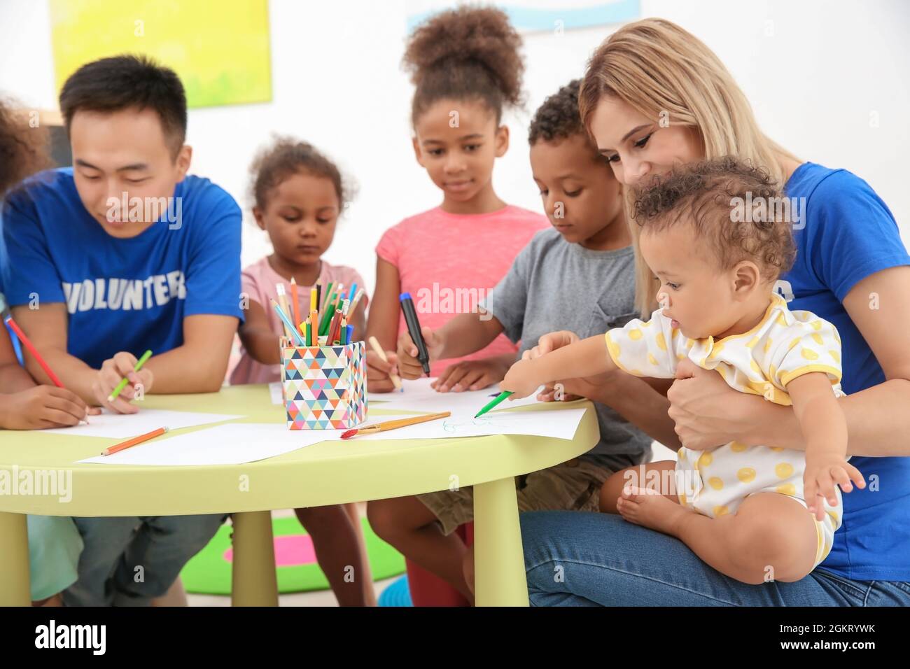 Young volunteers drawing with little children at table. Volunteering ...