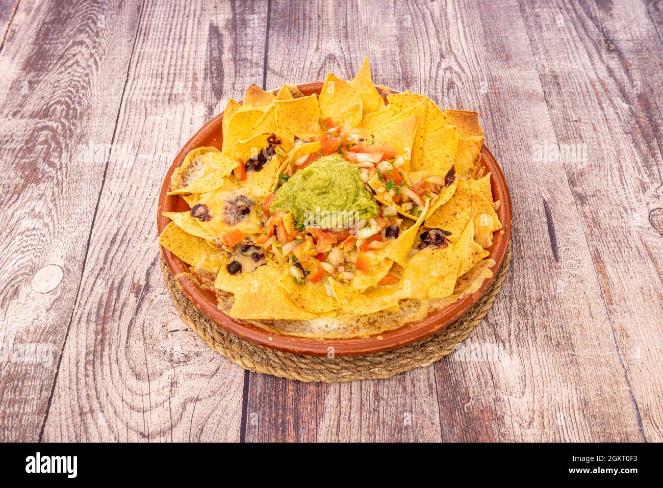 Clay plate with nachos, jalapeños, meat chili, cheese, guacamole ...