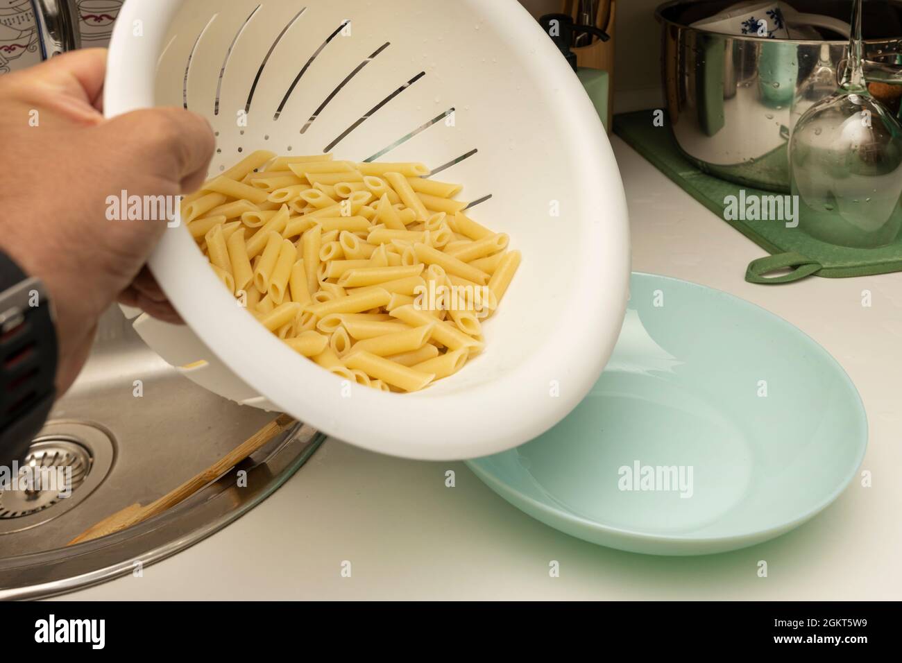 chef's hand pouring pasta from the dish drainer to later garnish with ...