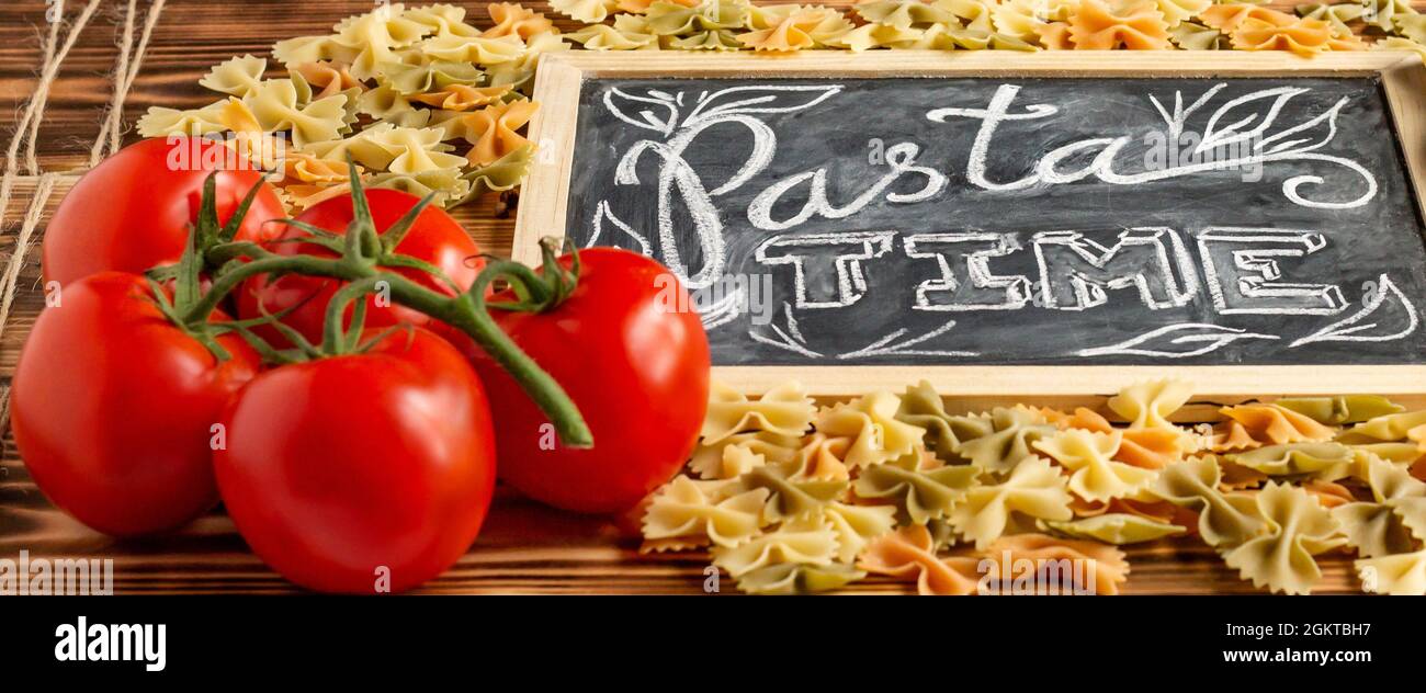 Chalk board sign Pasta Time on a wooden tabletop with raw farfalle ...