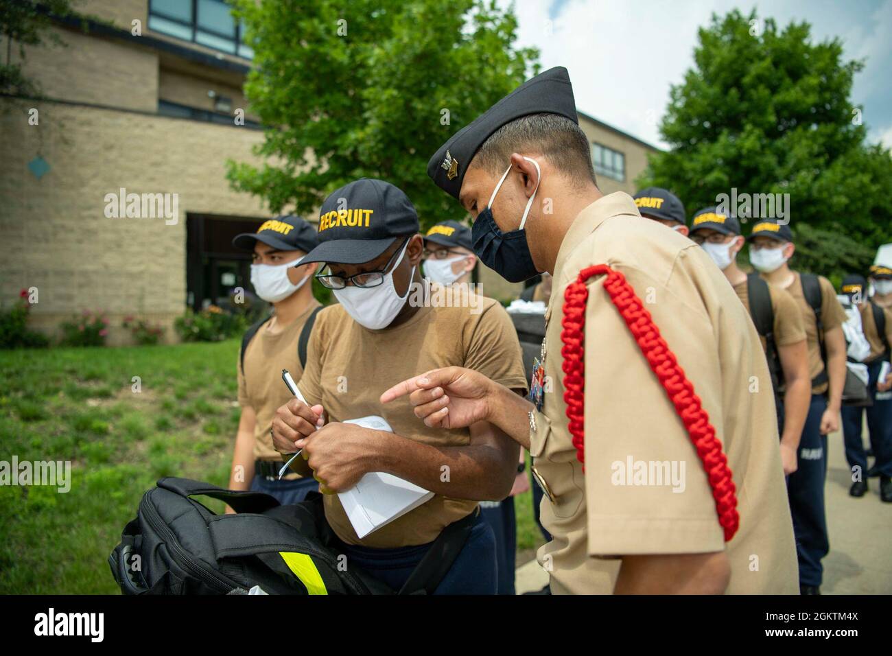 A recruit division commander assists a recruit in writing the correct ...