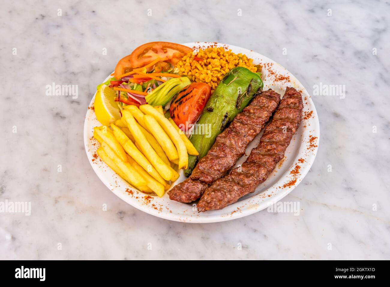 Plate of kofta kebab with roasted peppers, tomato chips and bulgur ...