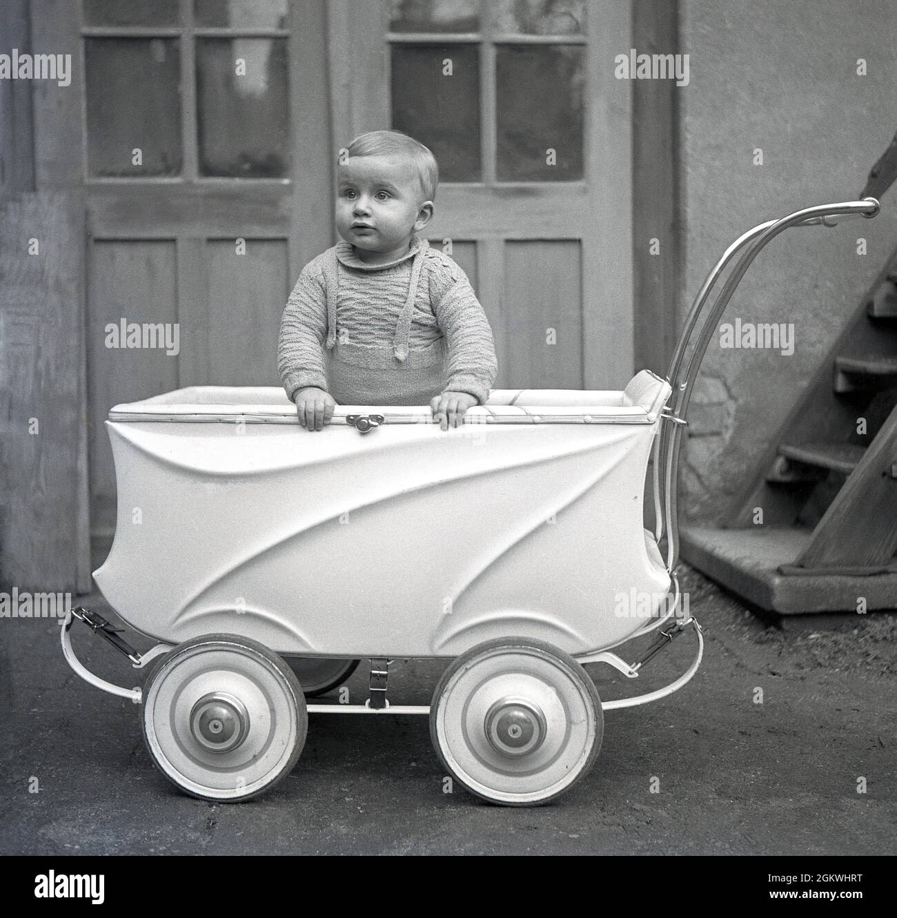 1950s, historical, outside in a courtyard, an infant child standing up ...