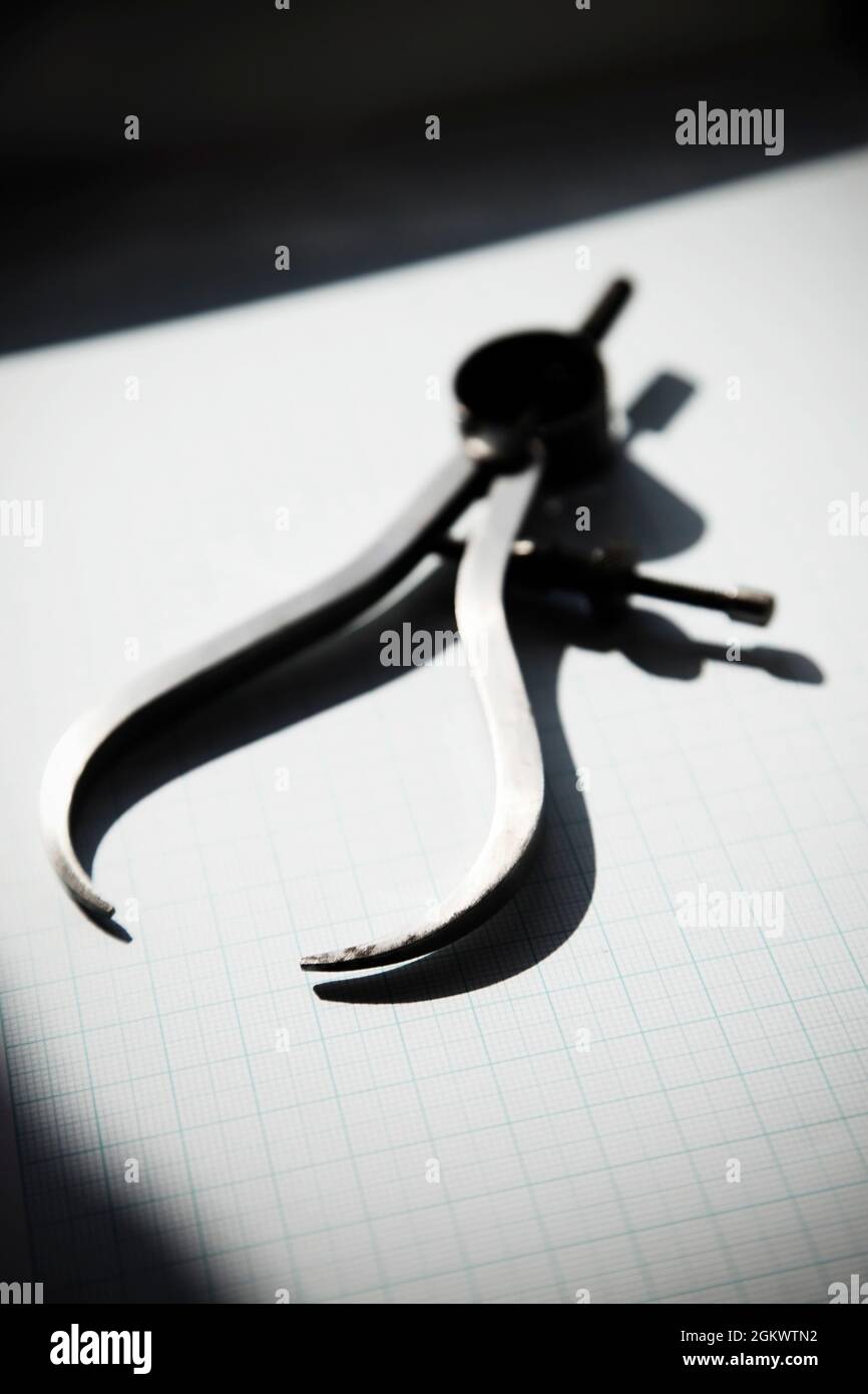 Metal outside spring calipers casting abstract shadow on piece of graph ...