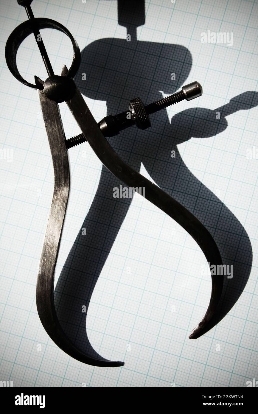 Metal outside spring calipers casting abstract shadow on piece of graph ...