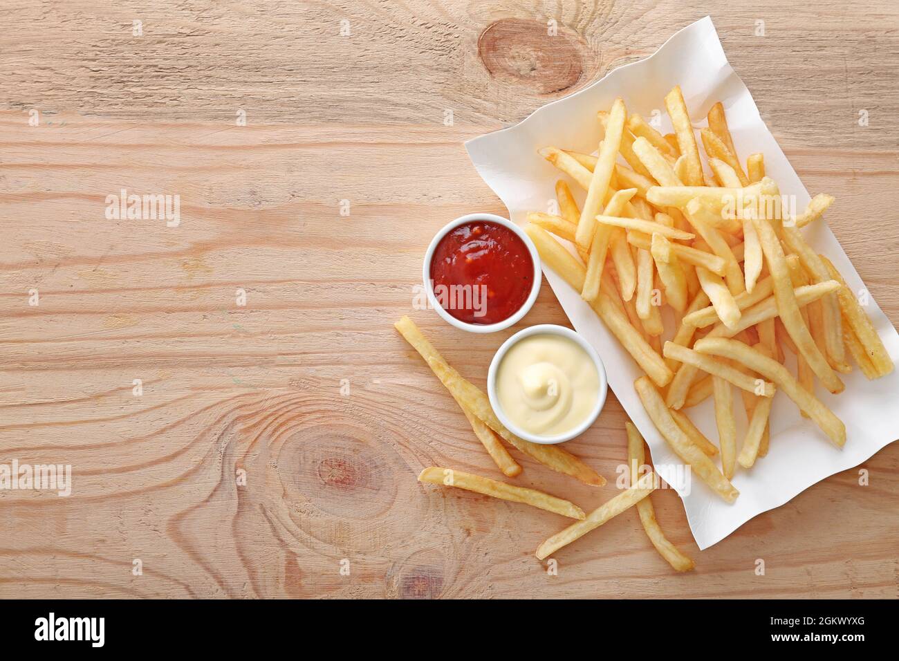 Yummy french fries in paper plate and bowls with sauces on wooden ...
