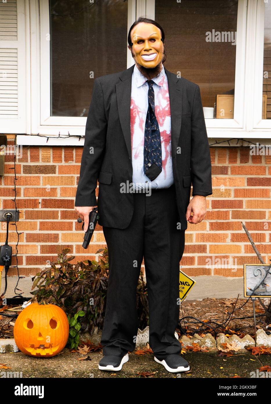 Vertical shot of a male in a scary bloody suit with a mask and a gun on ...