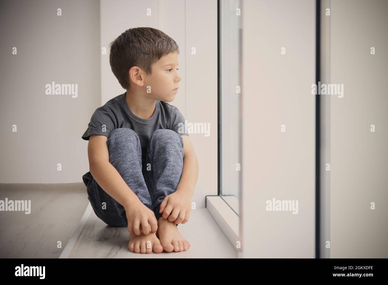 Sad lonely boy sitting on window sill at home Stock Photo - Alamy
