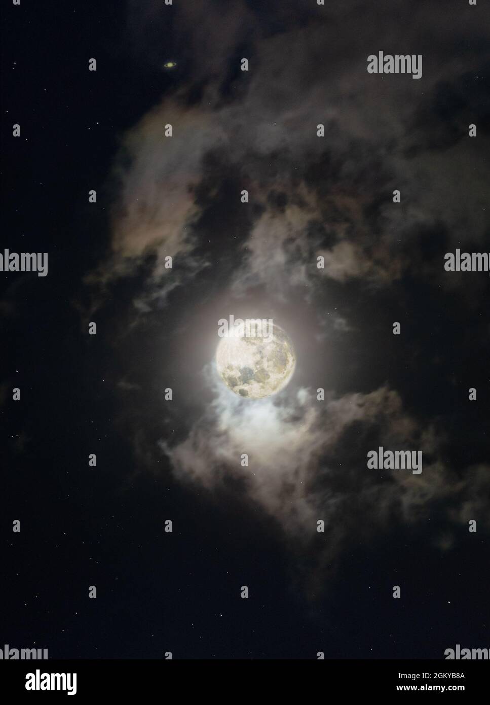 Vertical shot of the full moon and Saturn on a cloudy sky at night ...