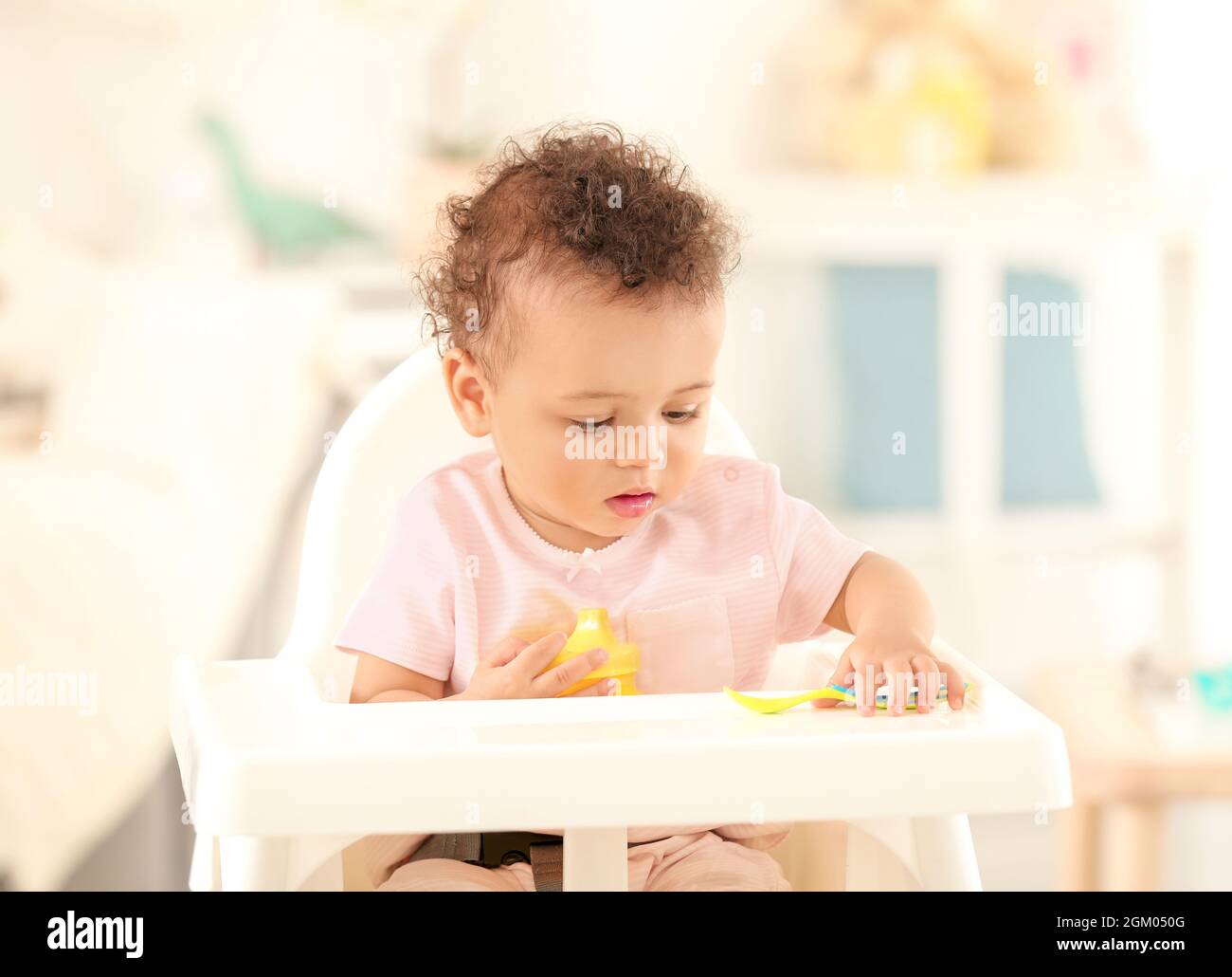 Cute baby with spoon sitting in room Stock Photo - Alamy