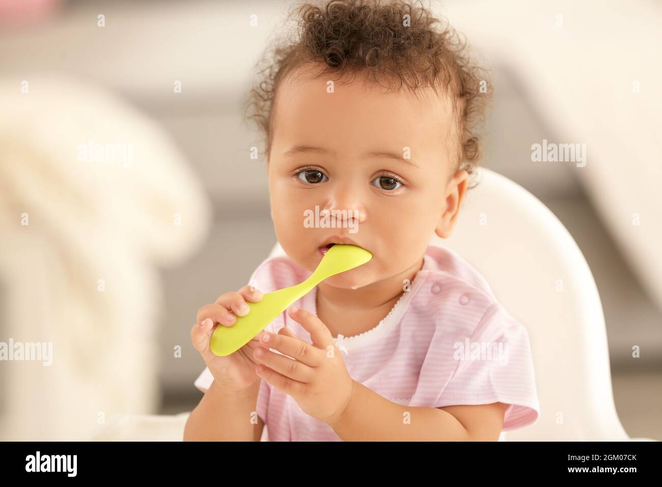 Cute baby with spoon sitting in room Stock Photo - Alamy