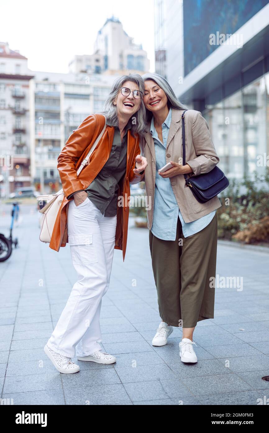 Stylish happy senior women stand on modern city street on autumn day ...