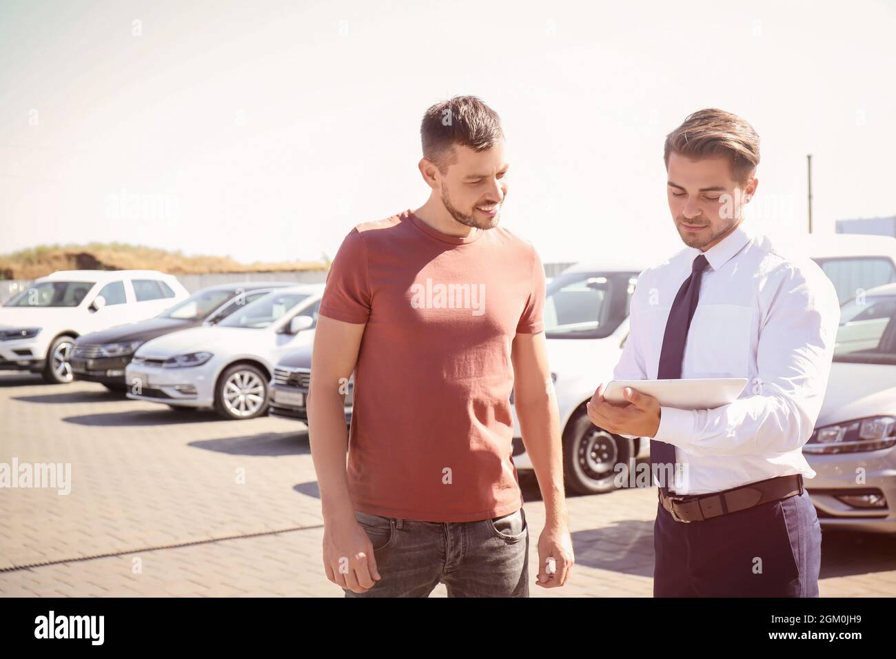 Salesman with tablet and customer standing near new cars outdoors Stock ...