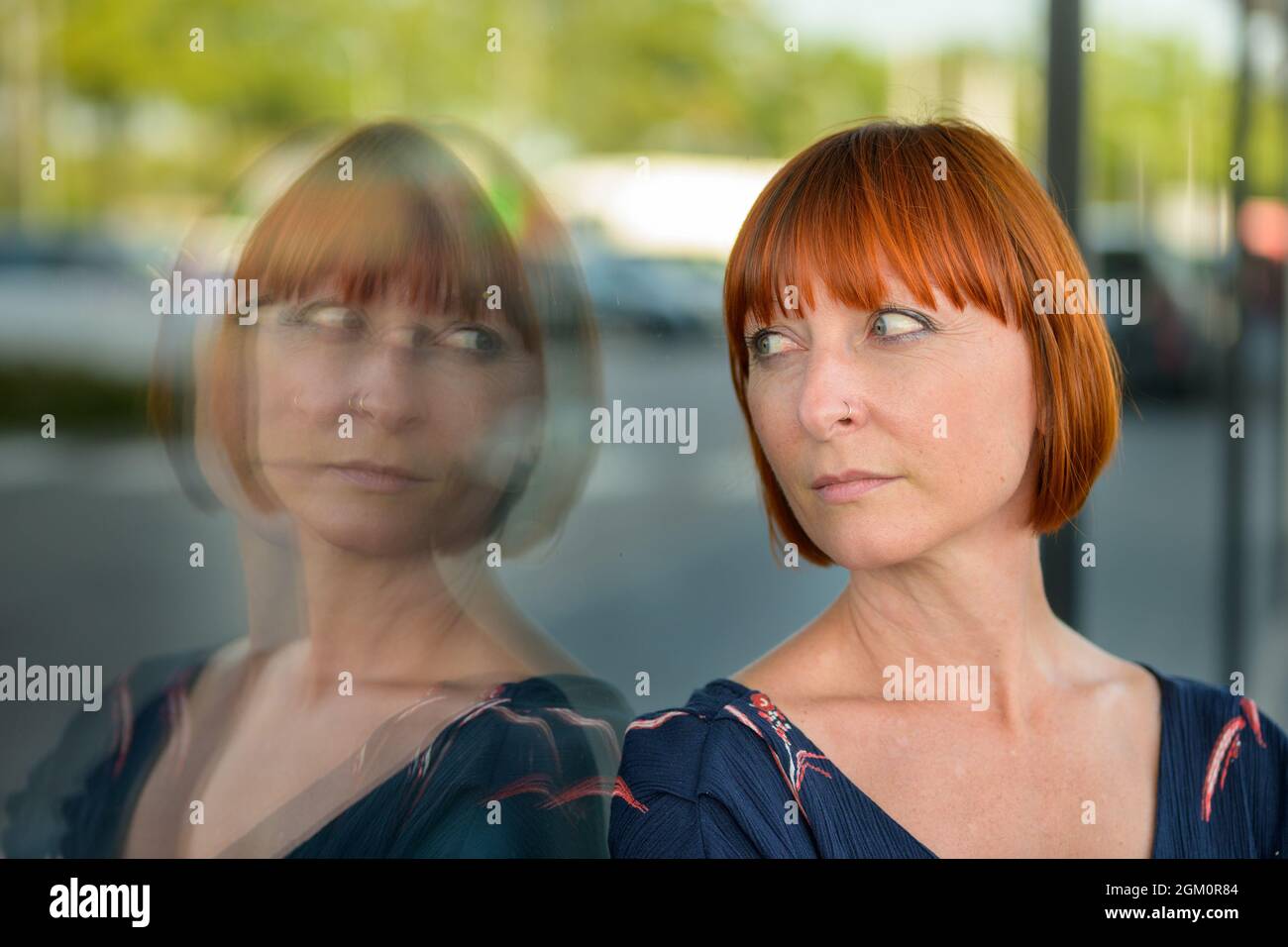 Woman looking back at her own reflection in the plate glass window of a ...